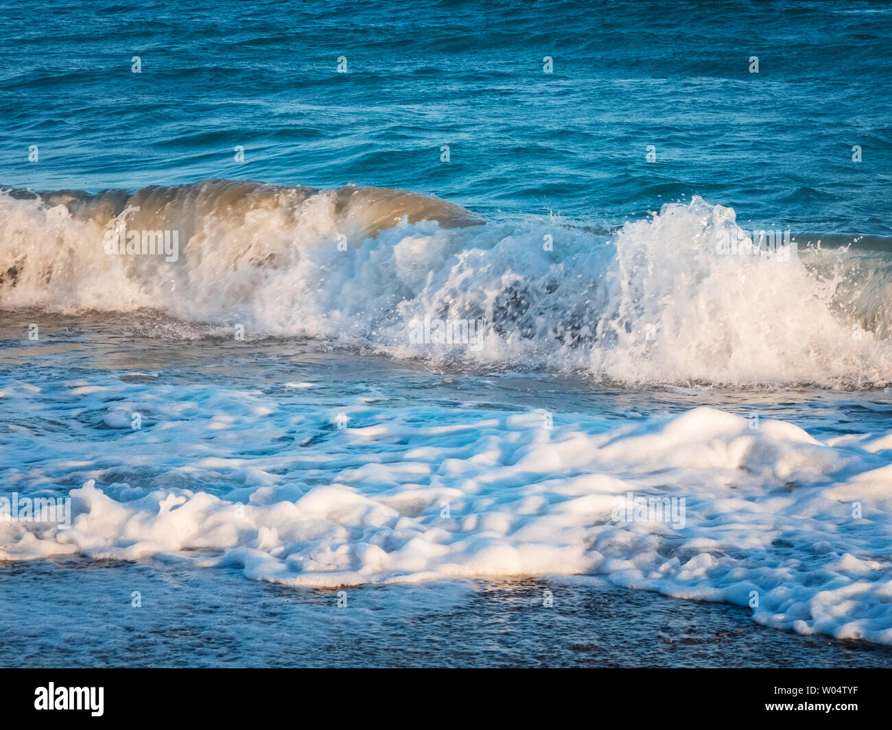 Splashing foamy waves of the sea beat on the pebble beach in the rays ...
