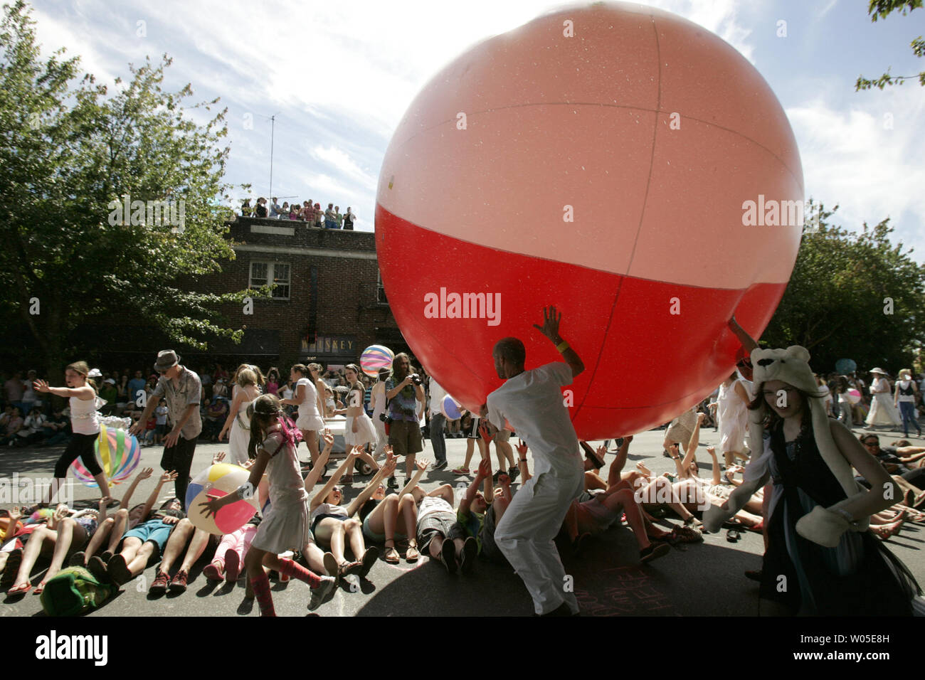 Parade goers lie on the pavement as a giant beach ball is rolled over ...