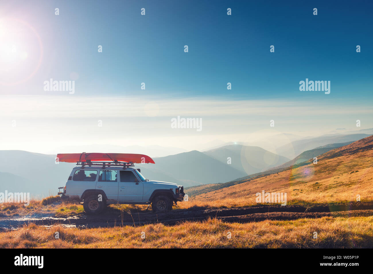 SUV car with kayak on the roof on a mountain trail. Vintage style shot ...
