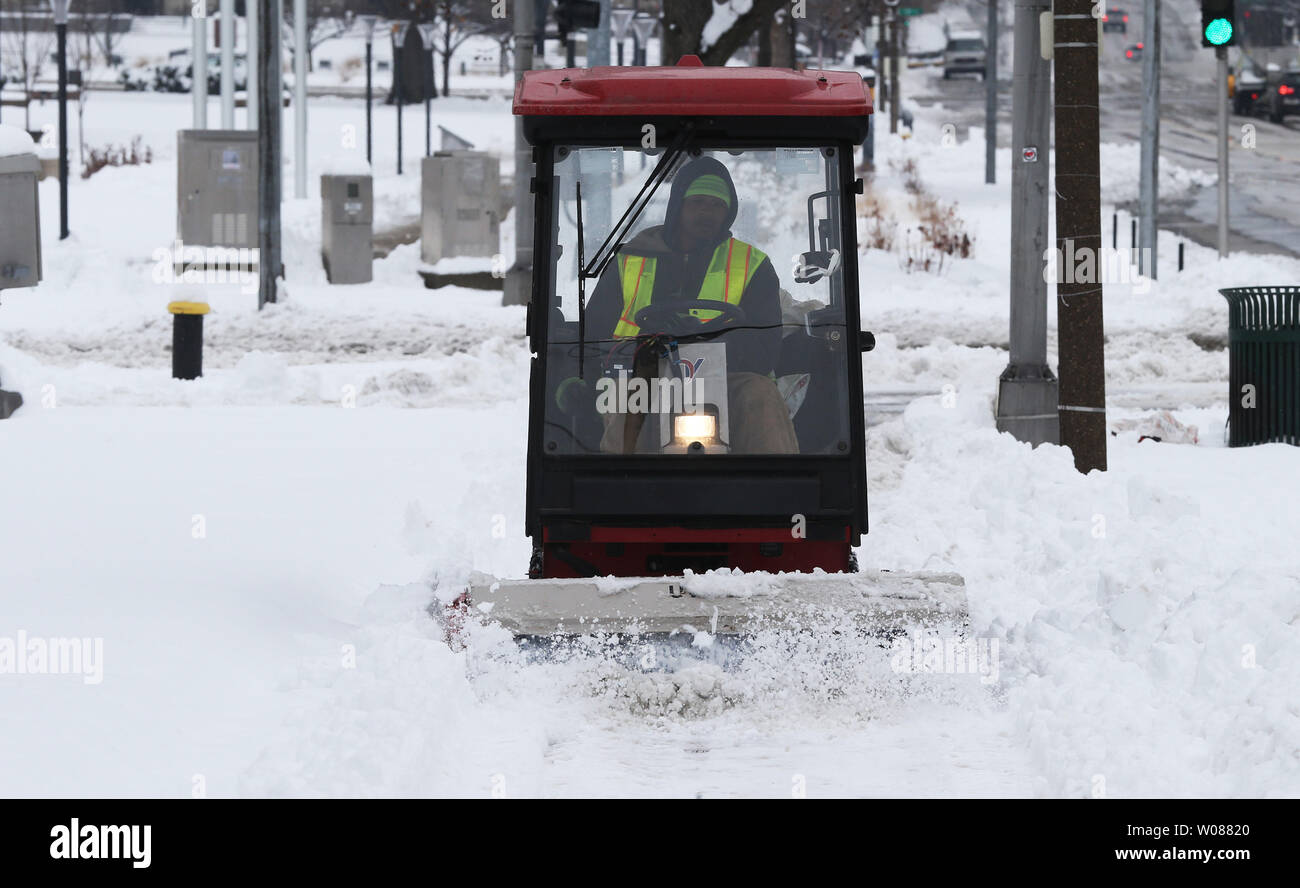 A city worker uses a brush machine to clear snow off the sidewalks in ...