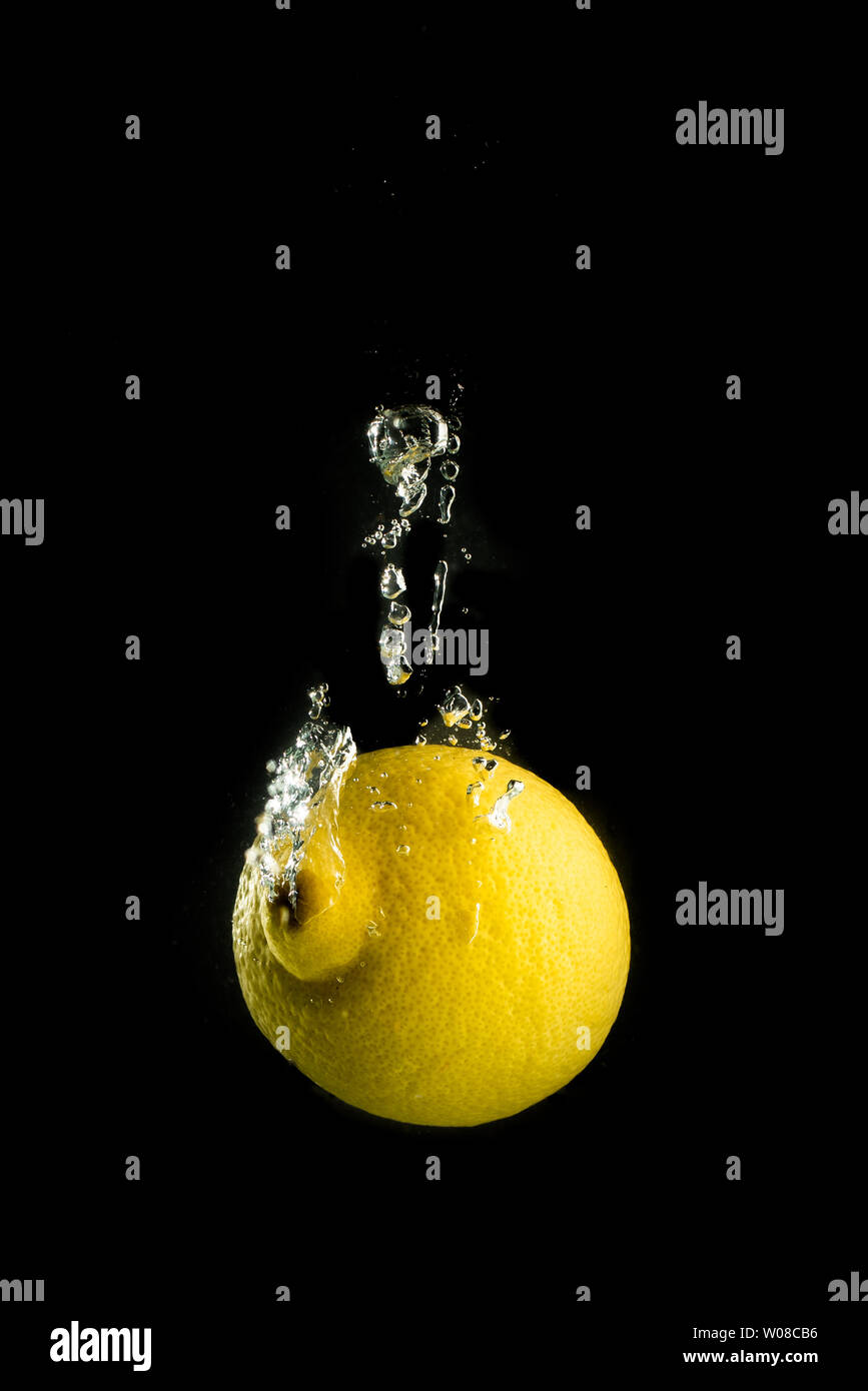 Lemon fruit splashing into water and sinking Isolated on black ...