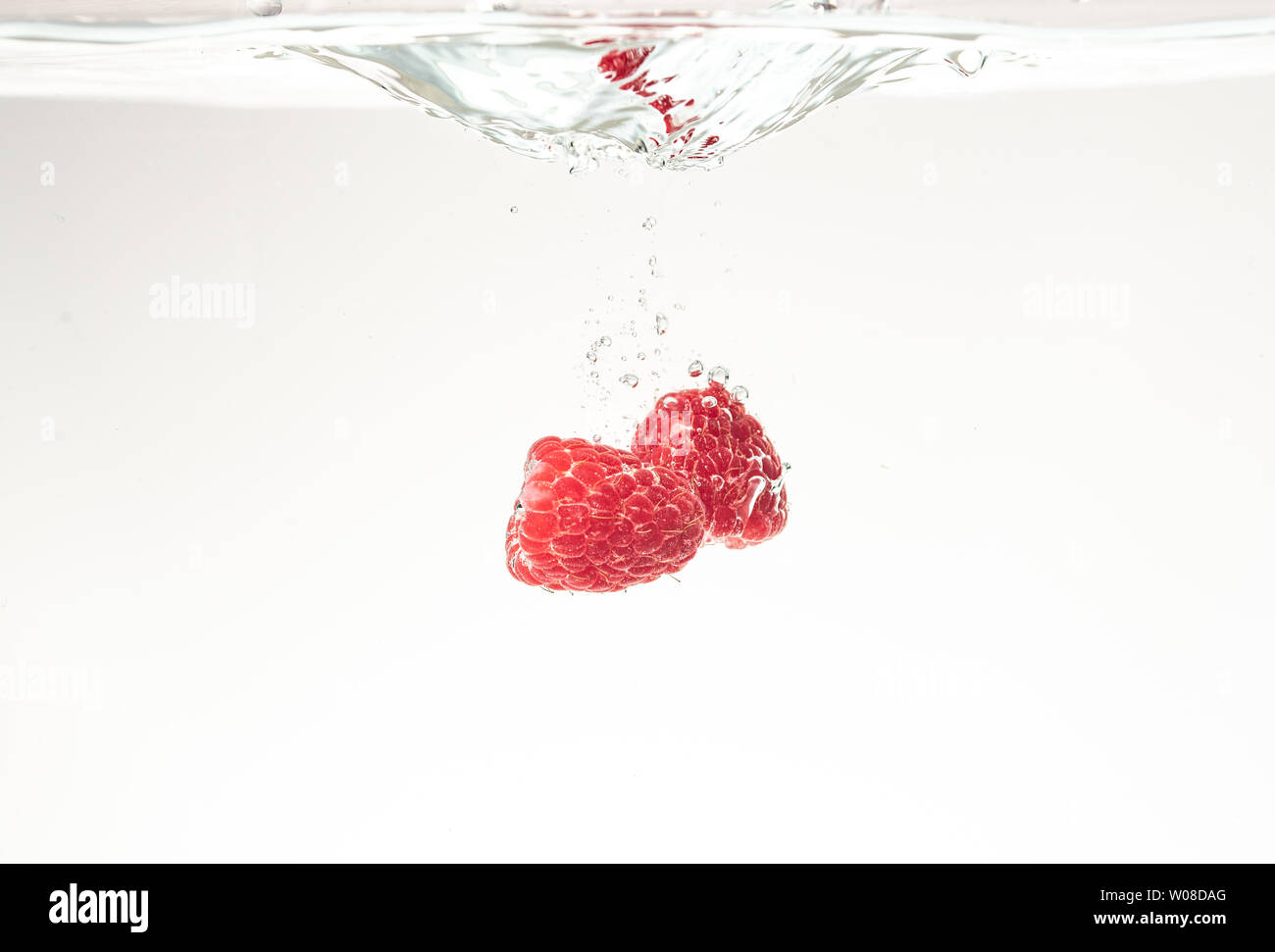 Raspberries splashing into crystal clear water with air bubbles ...