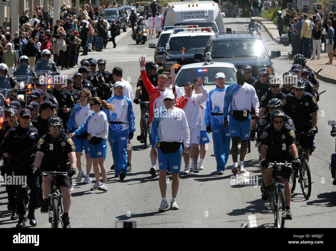 Olympic torch runners, in red, are surrounded by security as they run ...