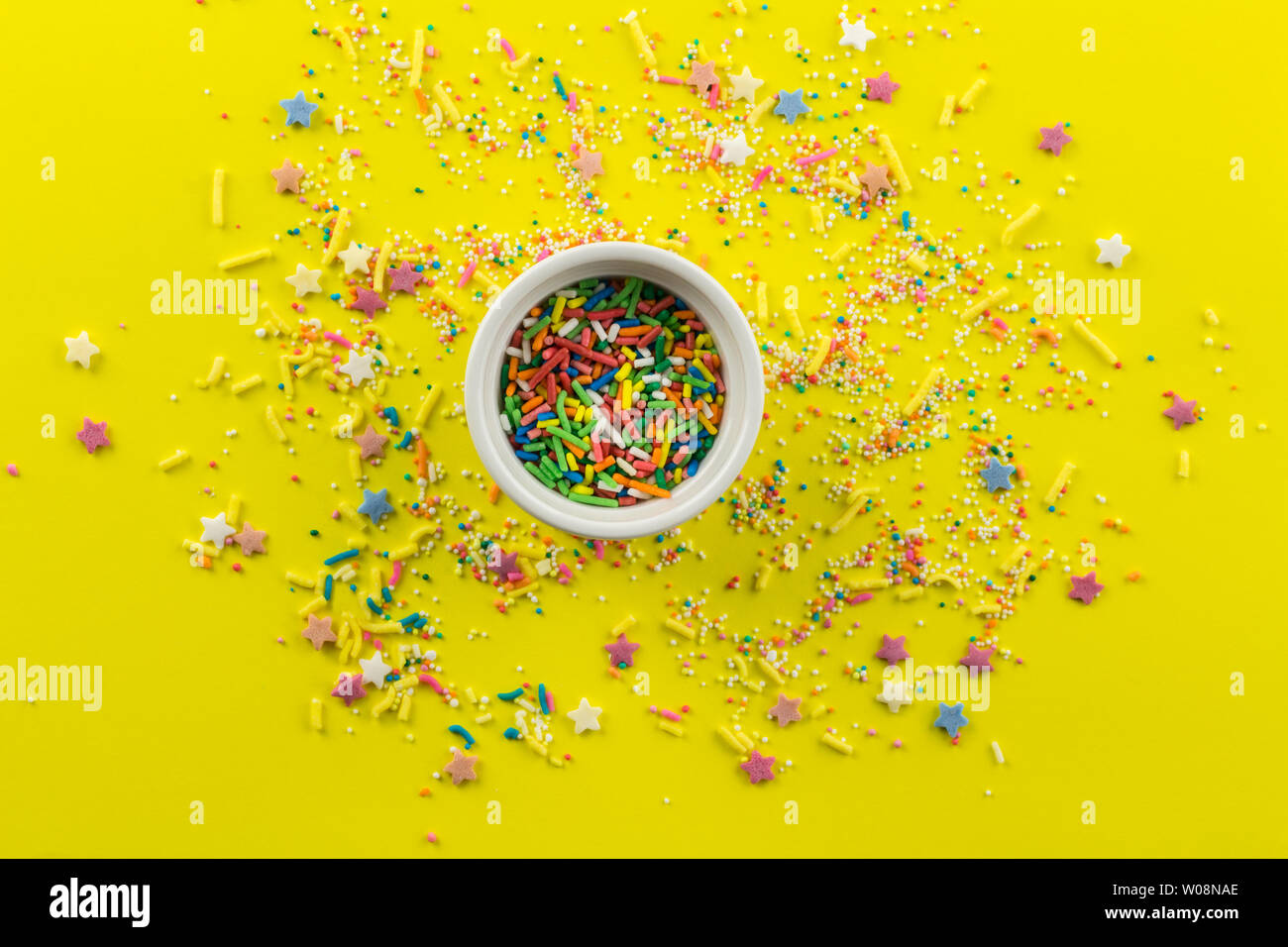 Sprinkles on yellow background with single little white bowl with multi ...