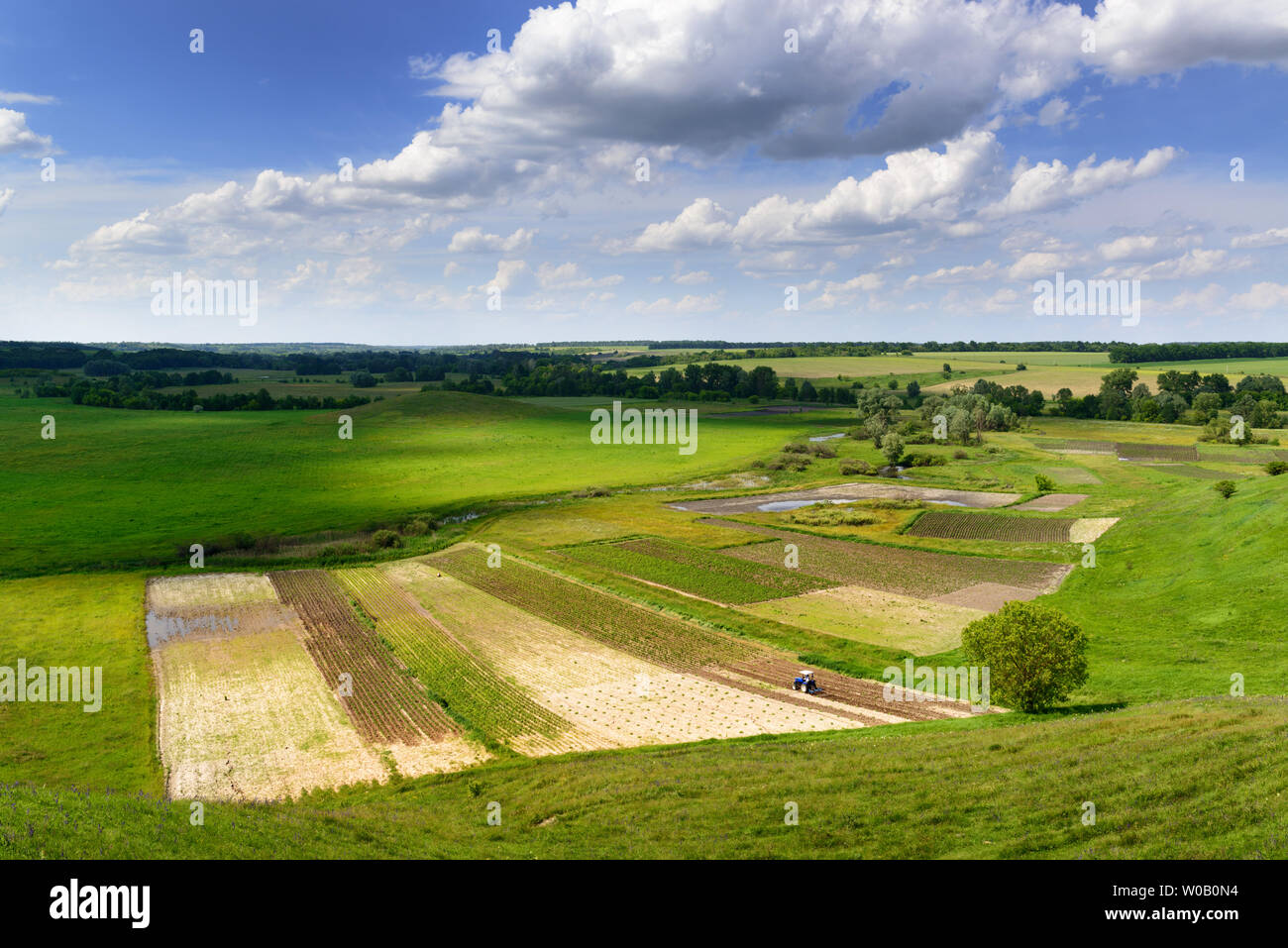 Beautiful countryside landscape with hills, fields and working tractor ...
