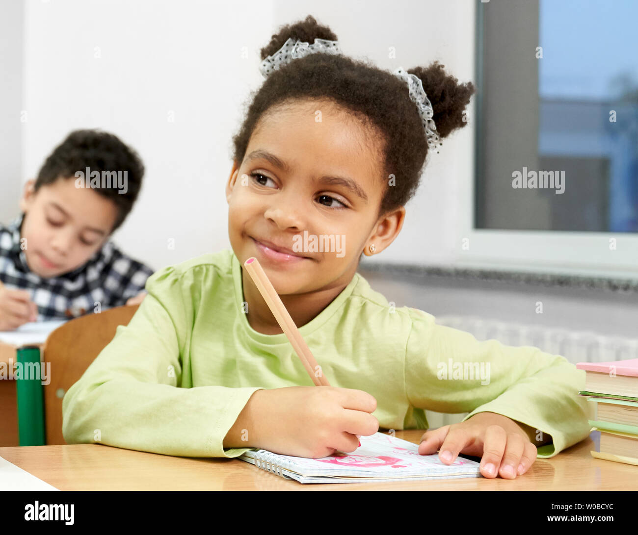 Pretty schoolgirl with curly hair holding in hand pen il, sitting at ...