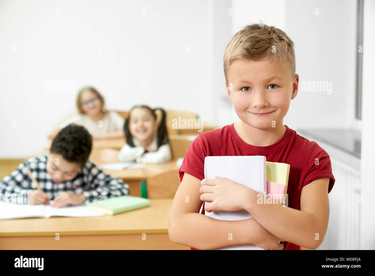 Handsome, young schoolboy standing, holding in hands books, looking at ...
