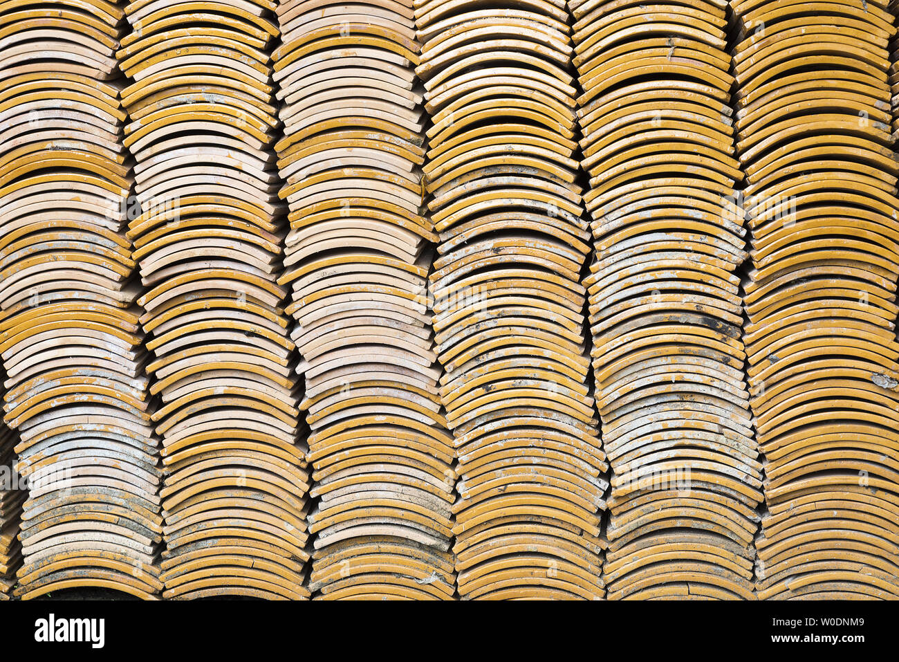 Stacks of yellow ceramic glazed curved roof tiles in a symmetrical ...