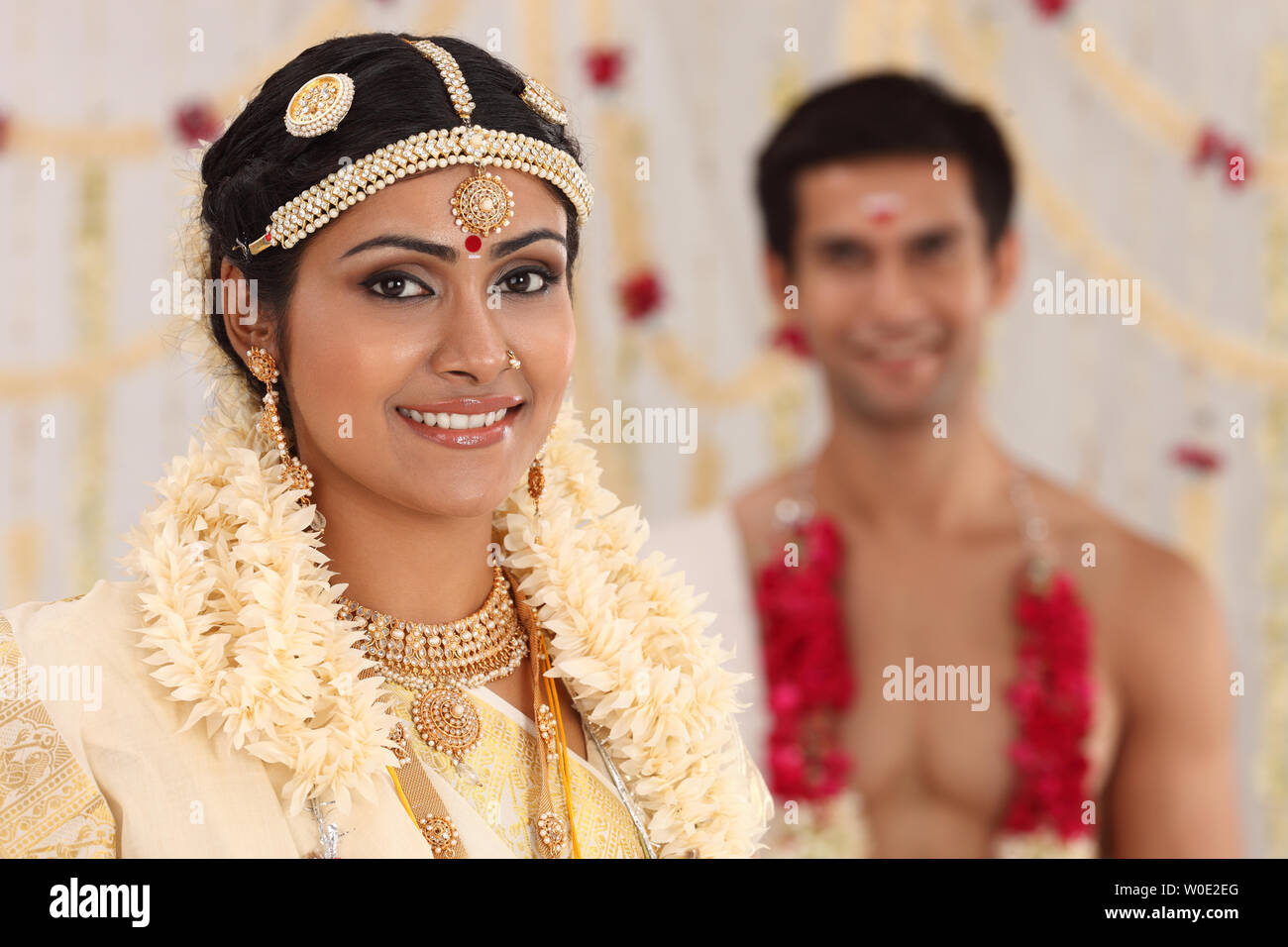 Portrait of an Indian bride smiling with her groom in the background ...