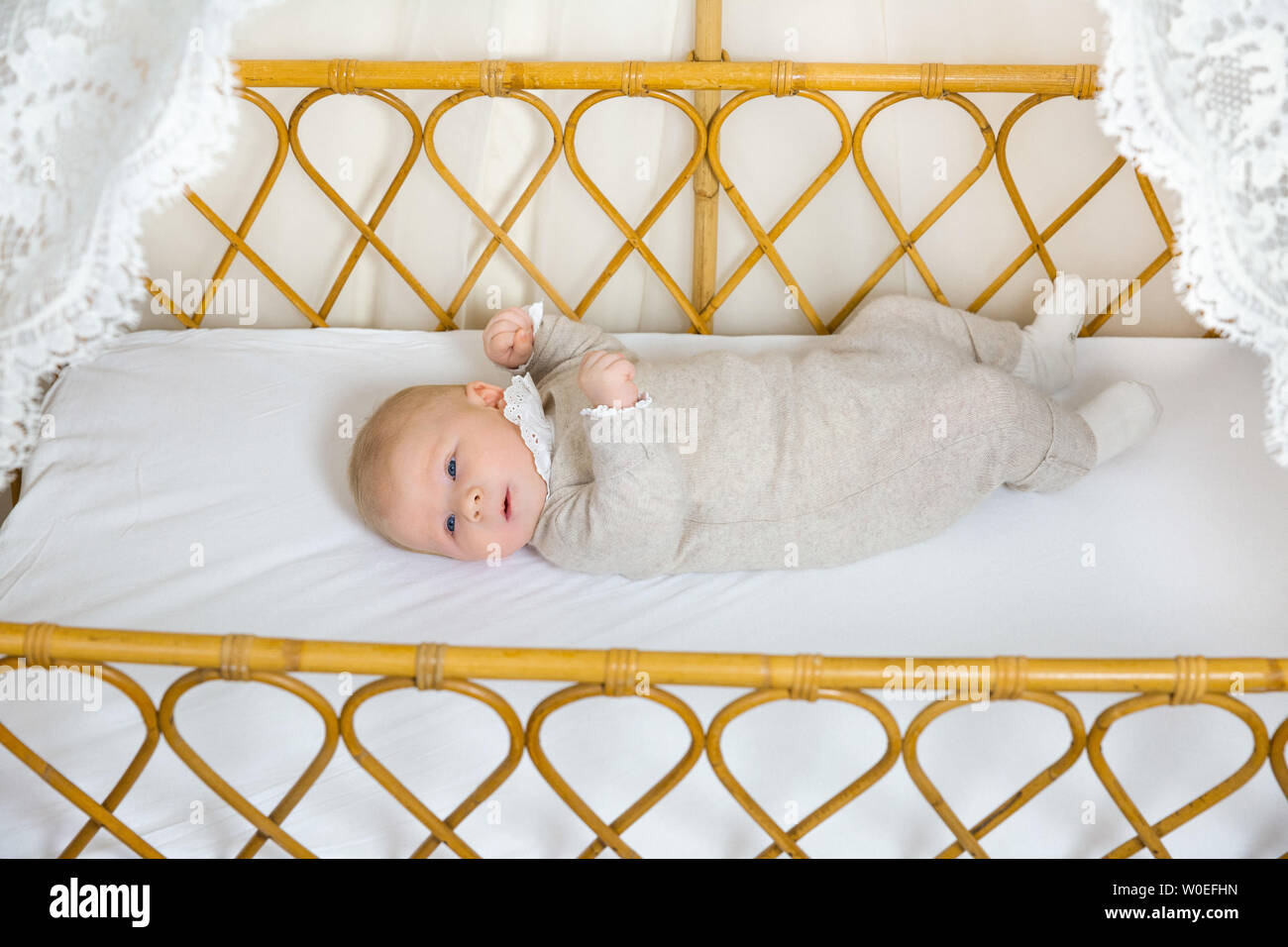 View of a baby of 2 months in beige layette lying on his back in his ...