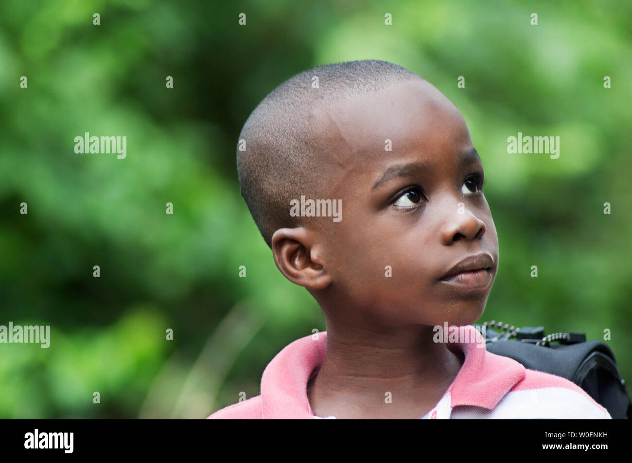 this child sitting next to a backpack looks aside on a green background ...