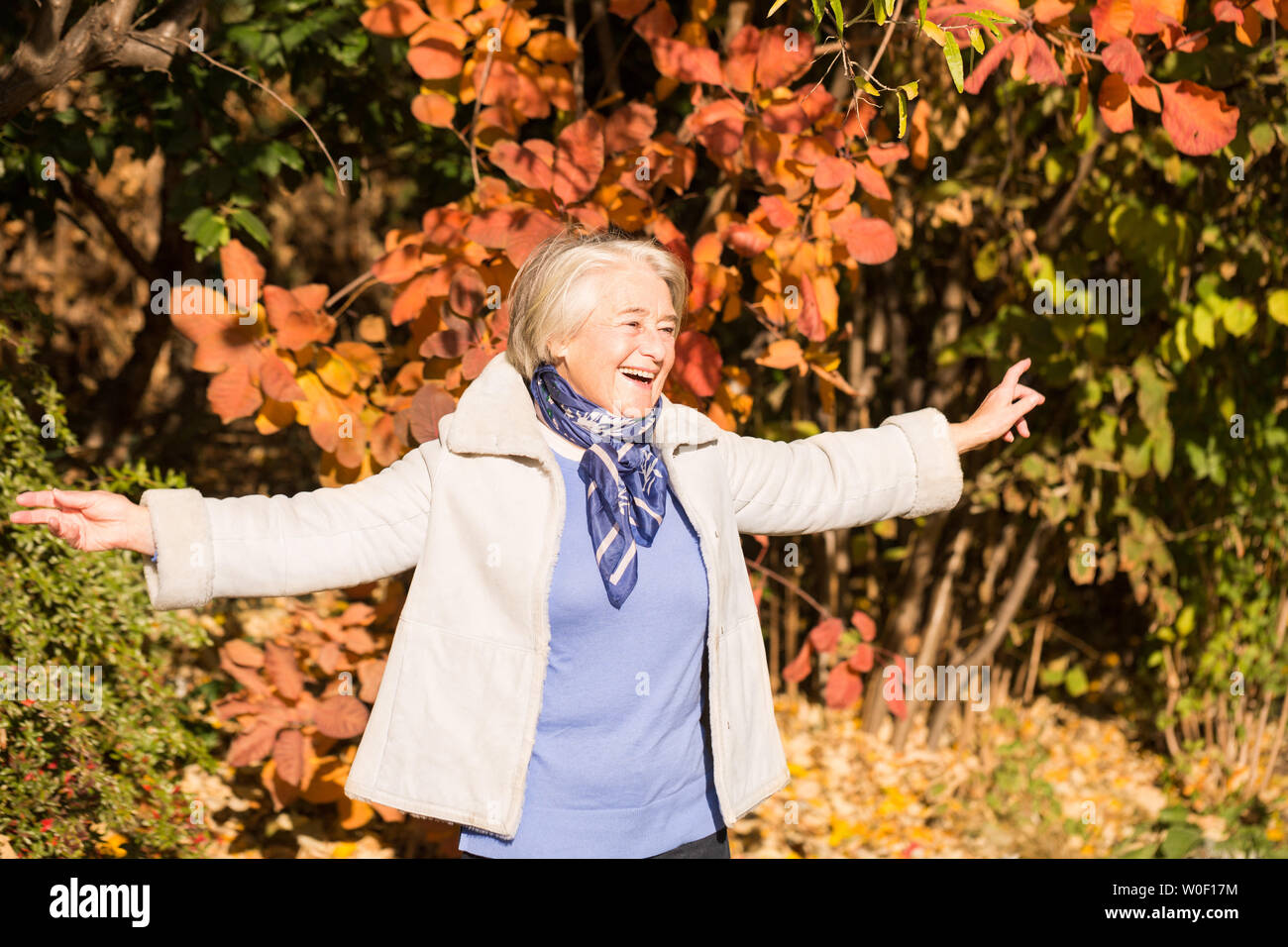 View of a pretty smiling grandma arms spread in nature in autumnal ...