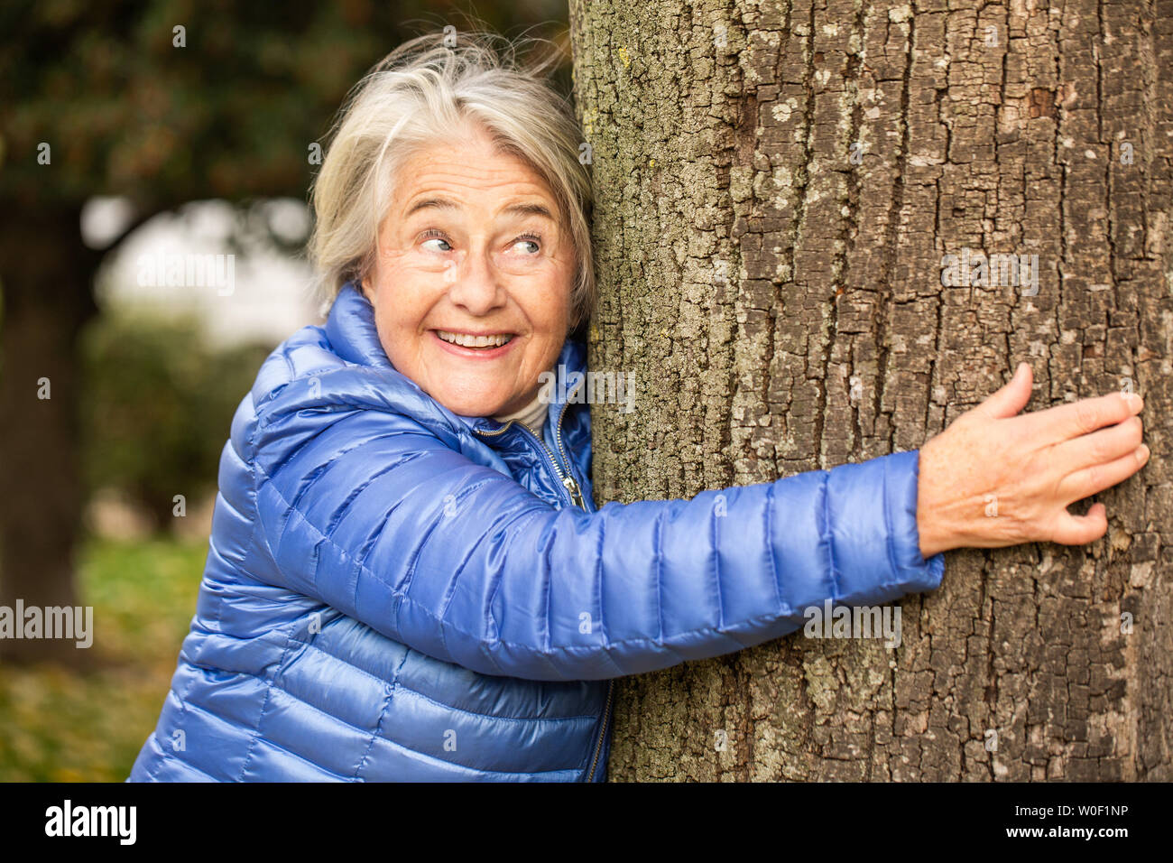 Portrait of a pretty senior woman hugging a tree Stock Photo - Alamy