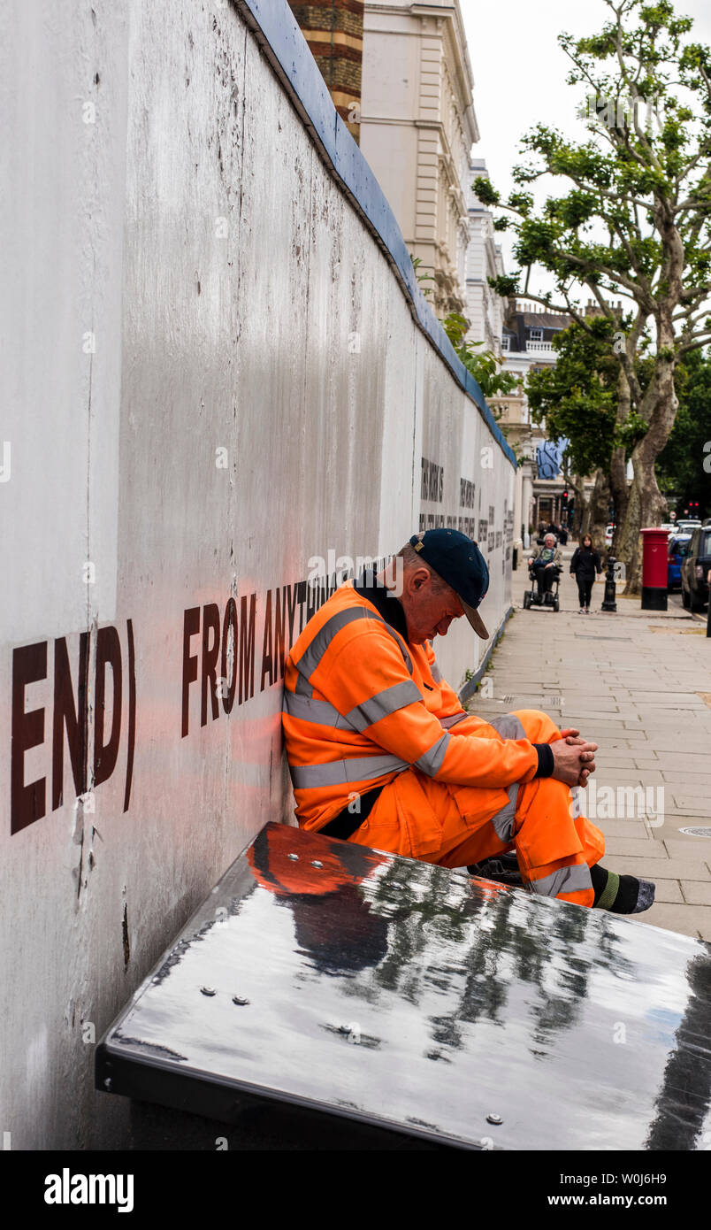 Workman taking a break outside construction site hoarding, London ...