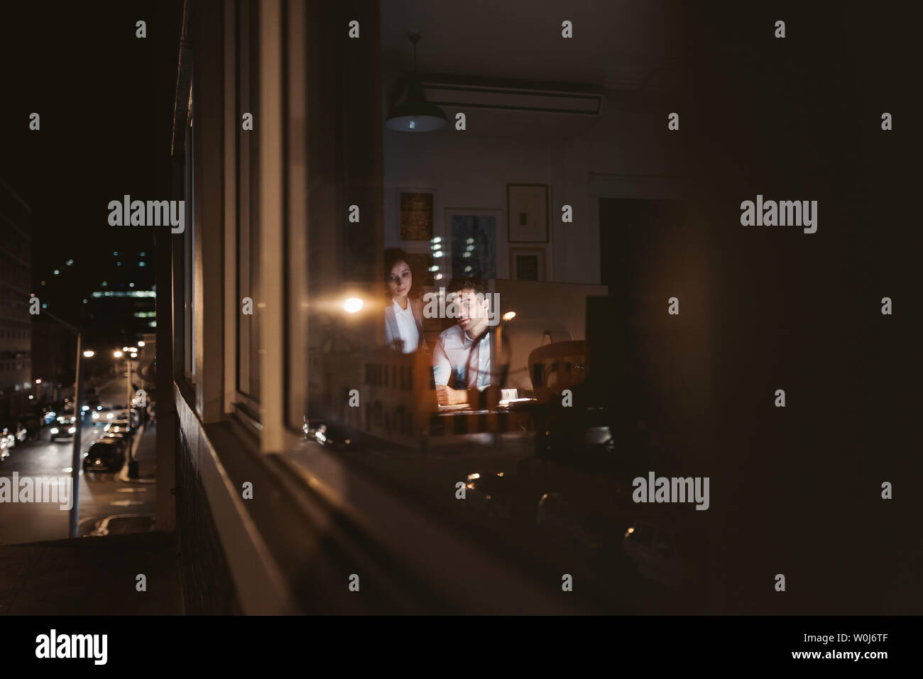 Two business colleagues working overtime together at a desk late at ...