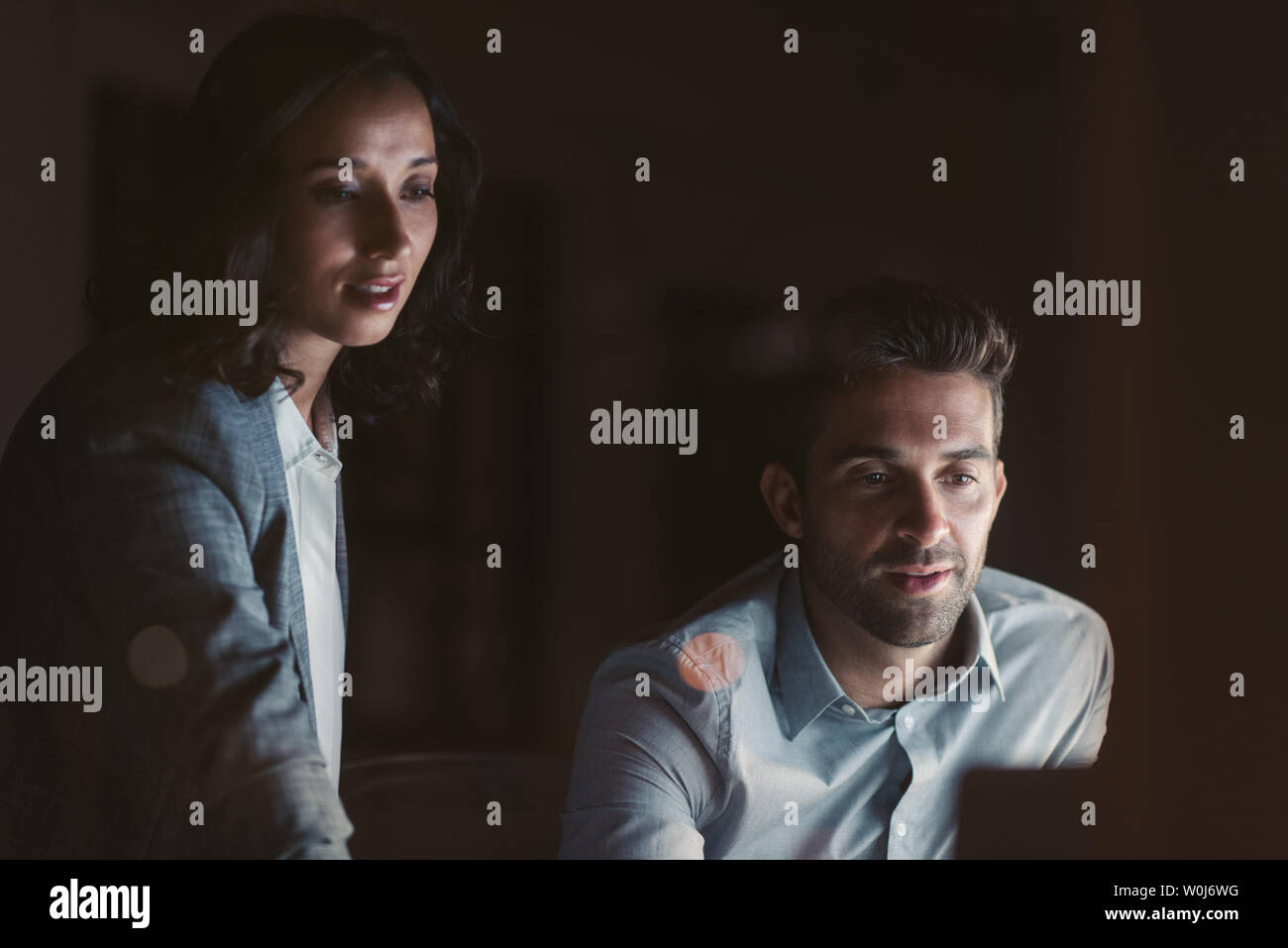 Two young businesspeople working overtime together on a computer at a ...