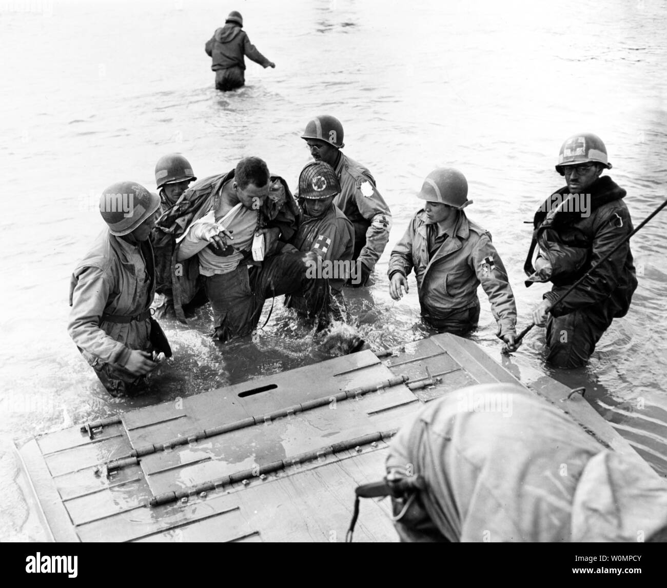 Medics help a casualty board a LCVP landing craft for evacuation from a ...