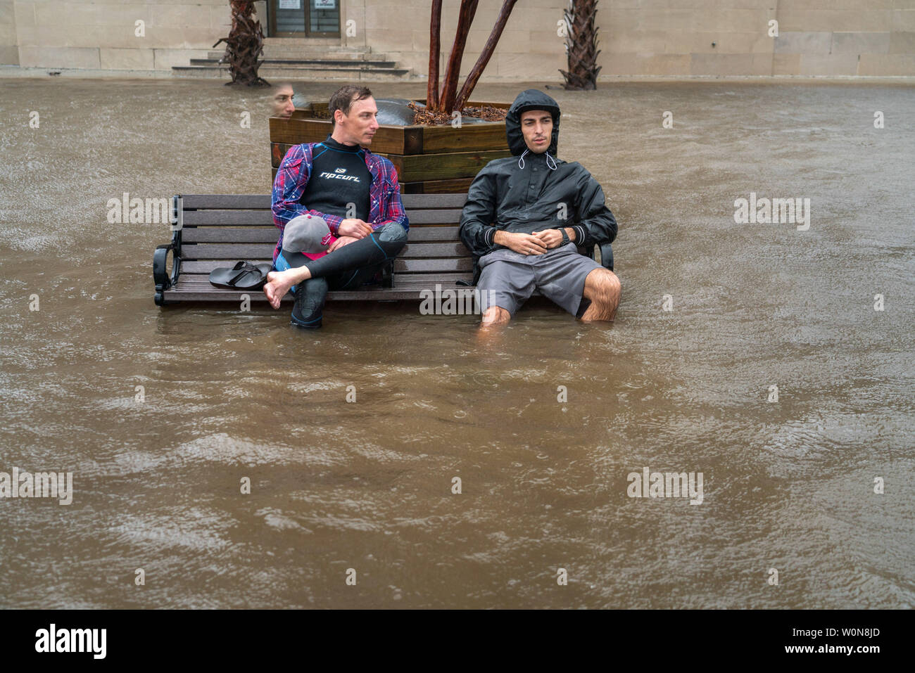 Chris Craig and Zach Boucher sit on a bench in the flooded waters edge ...