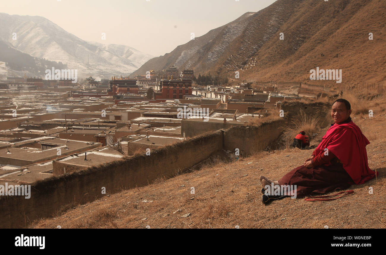 A Tibetan monk takes in the afternoon sun on a hilil overlooking the ...