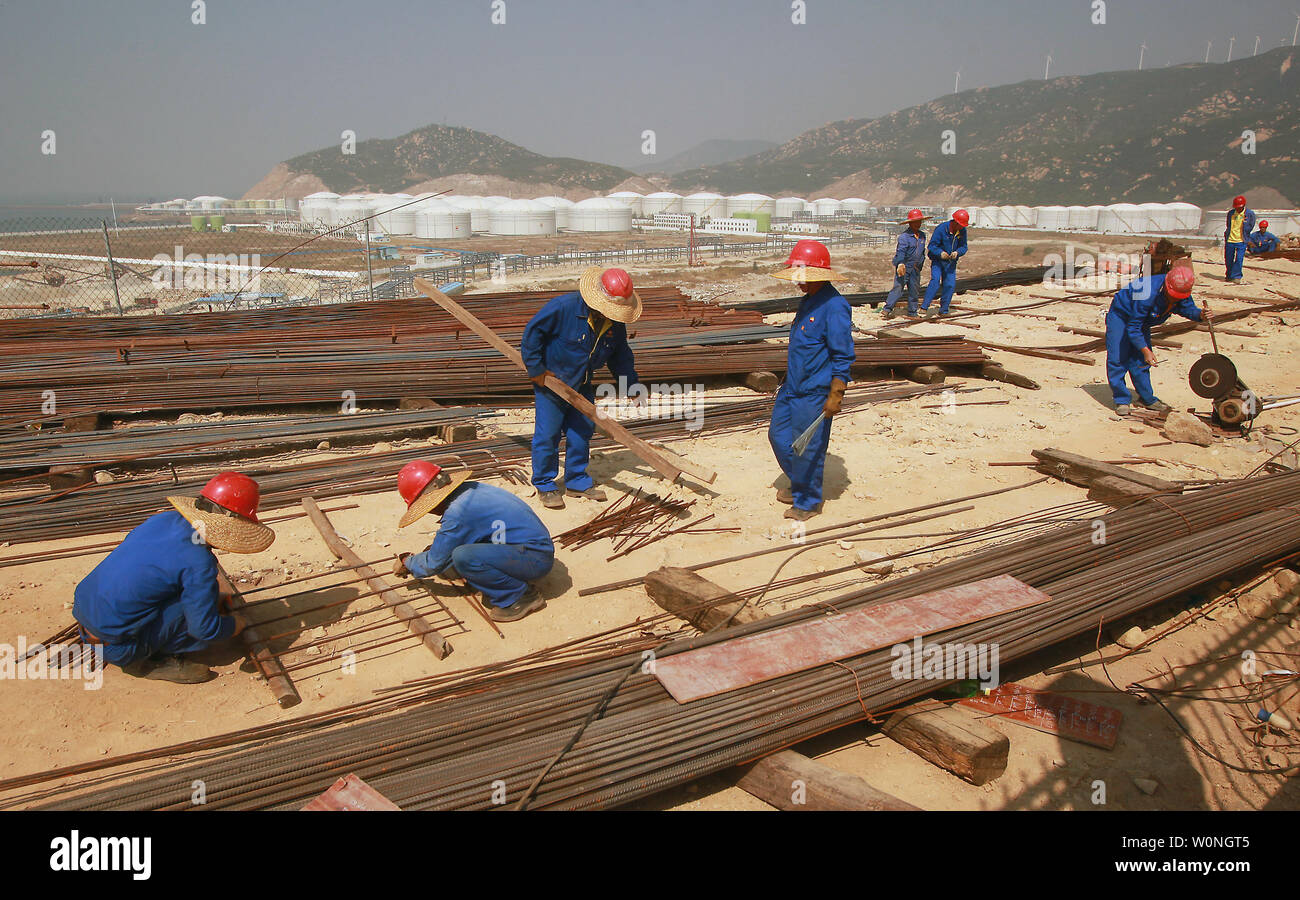 Chinese workers assemble rebar frames near a fuel storage yard and a ...