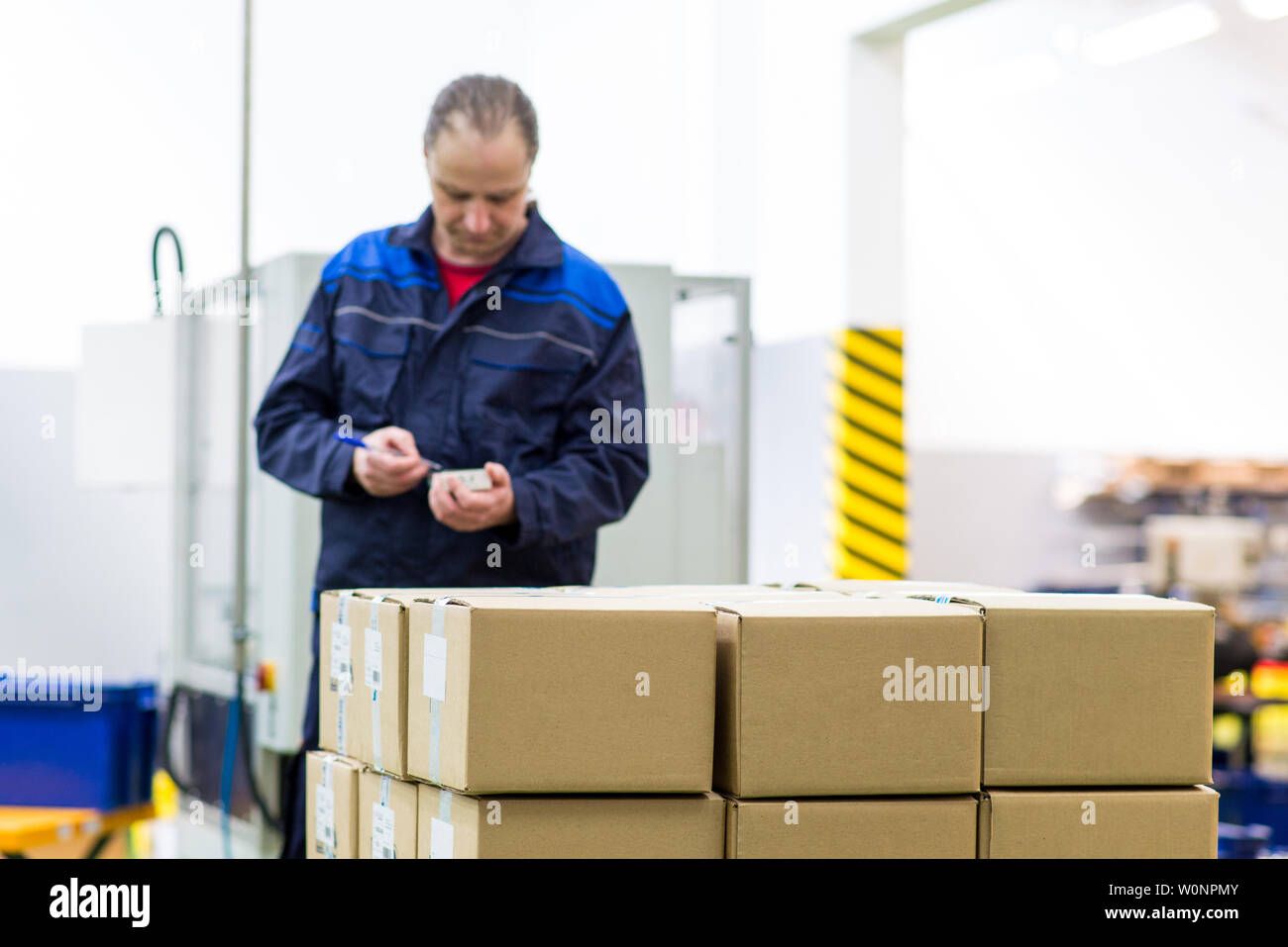 Factory worker taking notes while checking boxes in factory warehouse ...