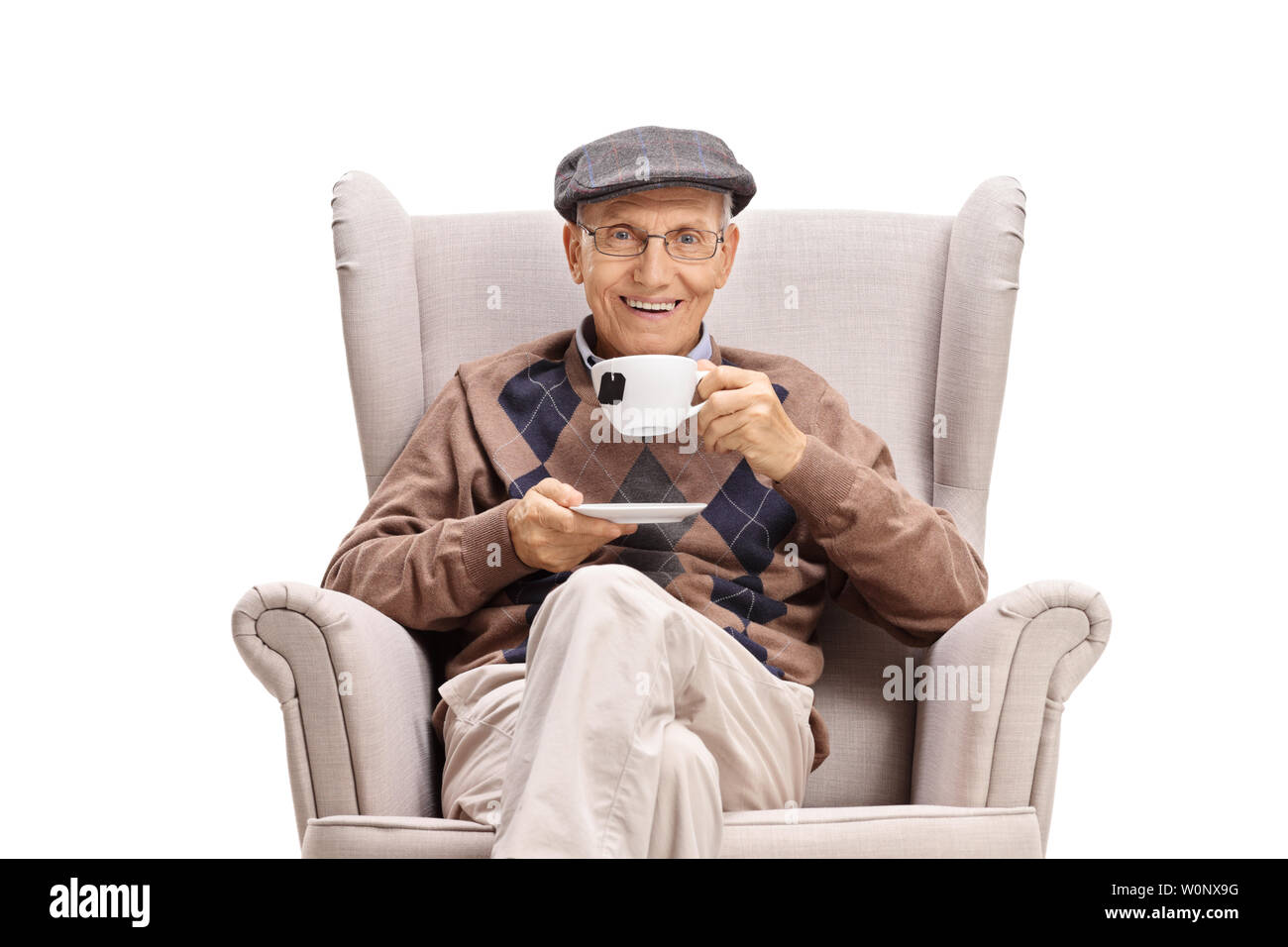 Elderly man sitting in an armchair and drinking a cup of tea isolated ...