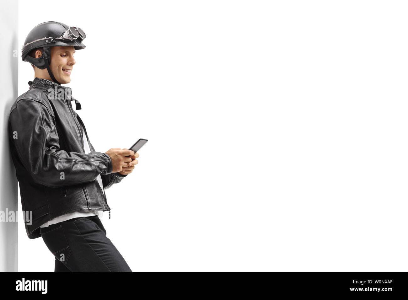 Young guy biker leaning against a wall and using a mobile phone ...
