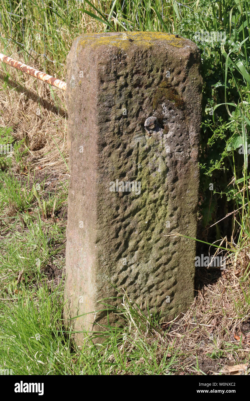 Old textured stone post on roadside grass verge with single rusty metal ...