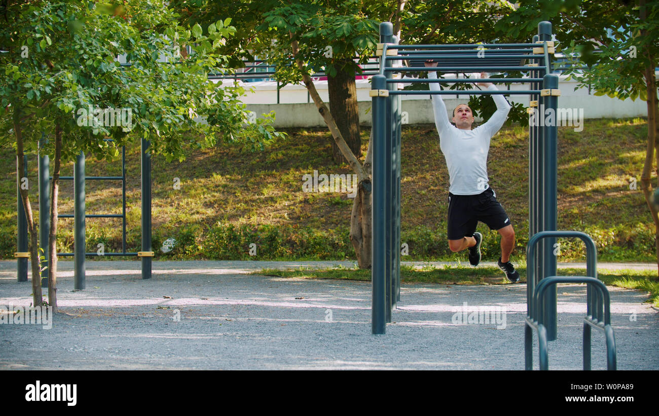 Man bodybuilder performs climbing on the horizontal bars - Mid shot ...