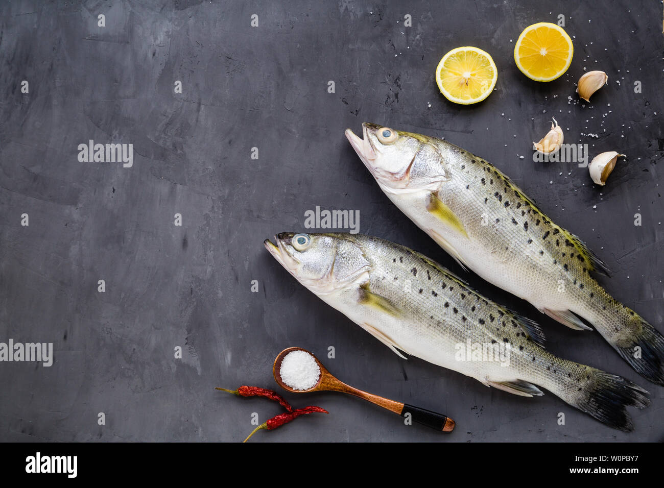 Fresh raw fish with spices, lemon, salt on dark stone background ...