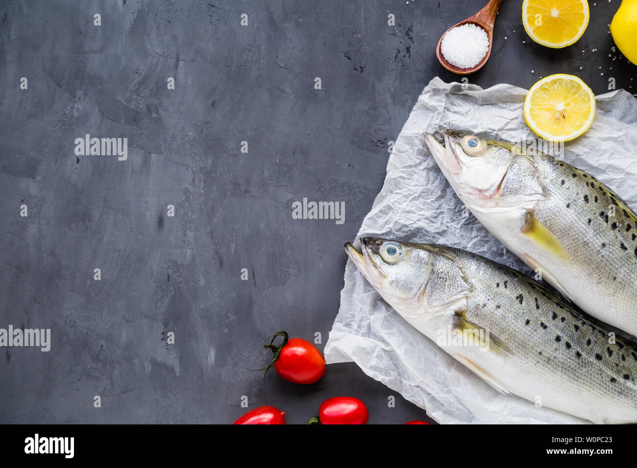 Fresh raw fish with spices, lemon, salt on dark stone background ...