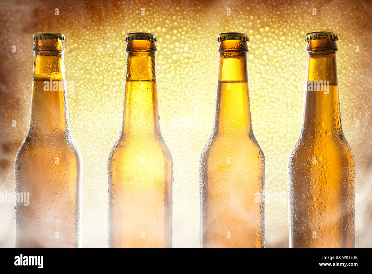 Row of four closed glass bottles with fresh beer on golden background ...