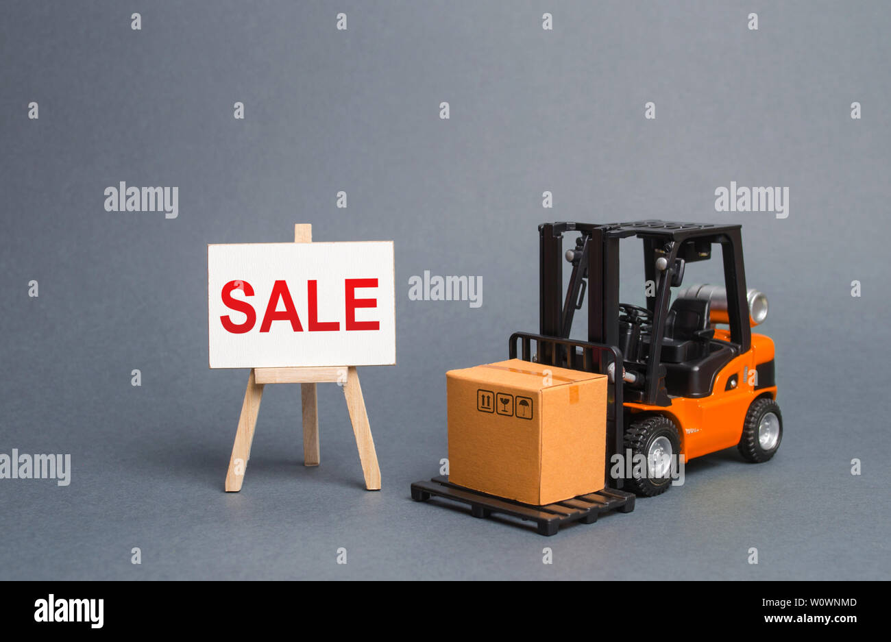Orange forklift truck carries a cardboard box and a stand with a word ...