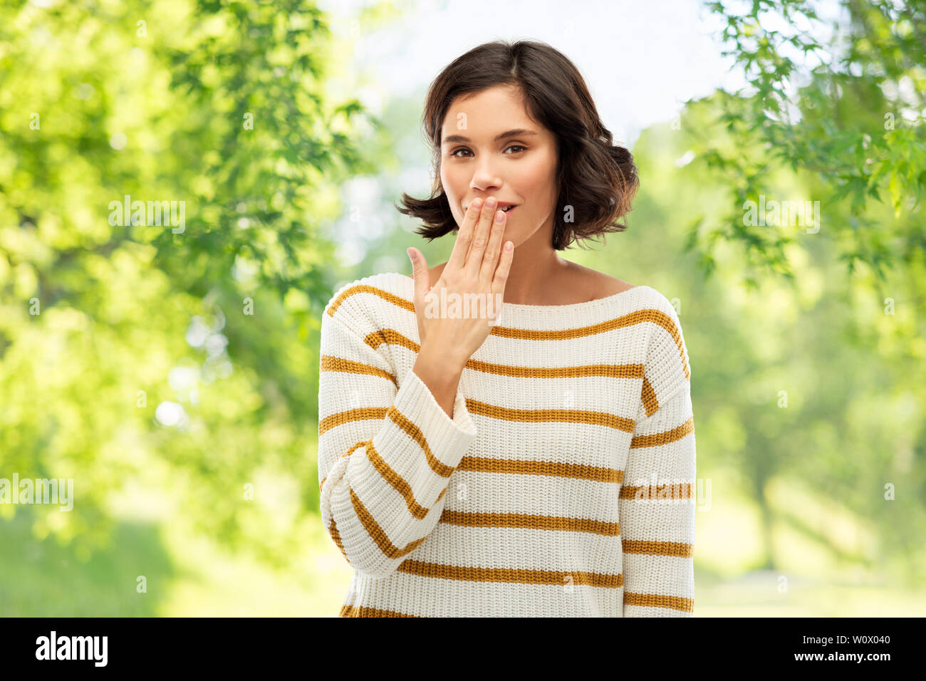 woman covers mouth by hand over natural background Stock Photo - Alamy