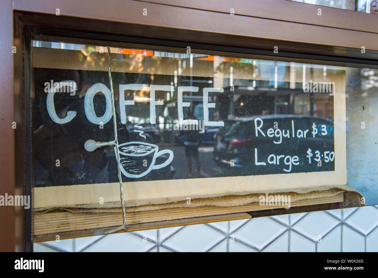 A chalkboard sign in a shop window on a busy street advertising coffee ...
