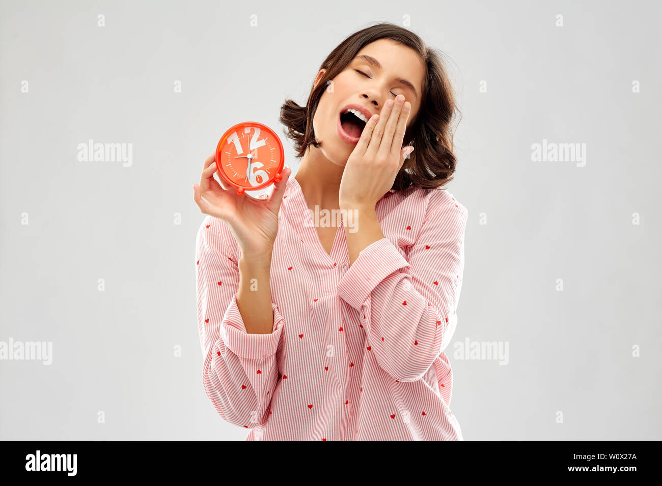 sleepy woman in pajama with alarm clock yawning Stock Photo - Alamy