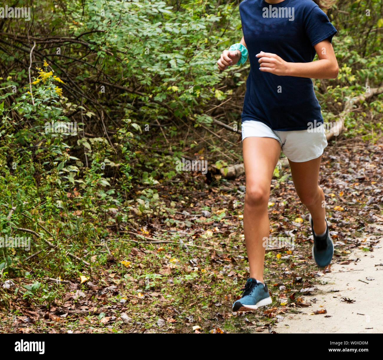 A female distance runner is running on a dirt and grass path with ...