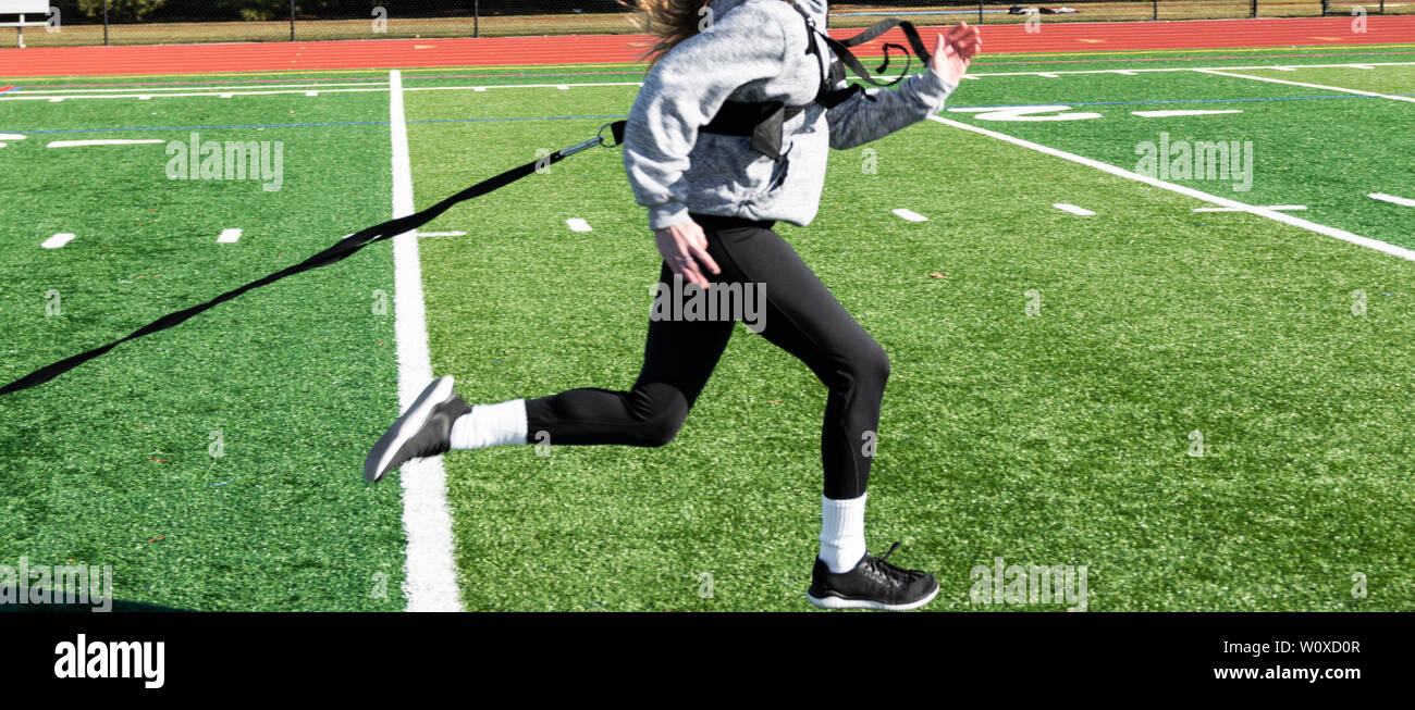 Side view of a female high shool runner sprinting on a green turf field ...