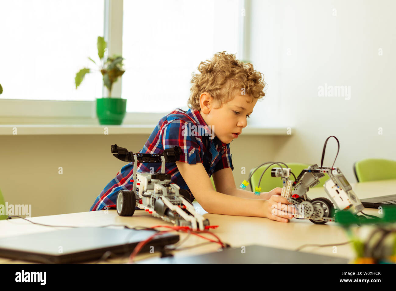 Being focused. Serious cute boy standing at the table while being ...