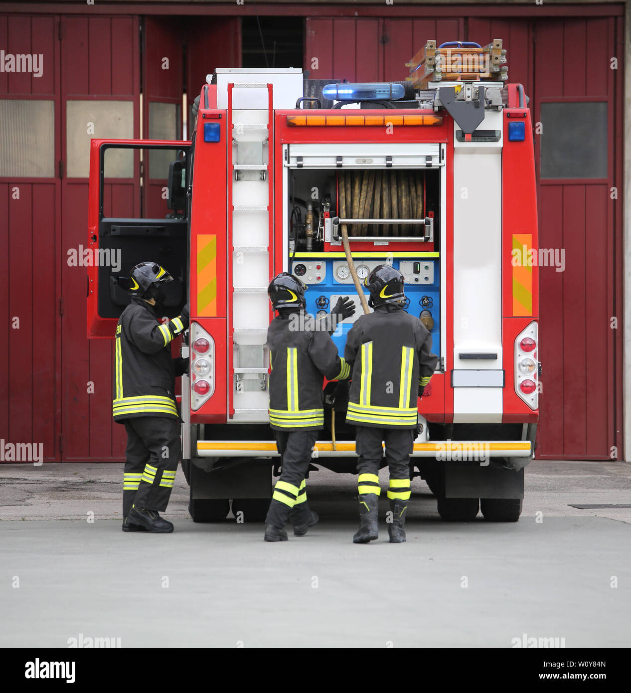 three firefighters with uniform in action and the fire engine during a ...