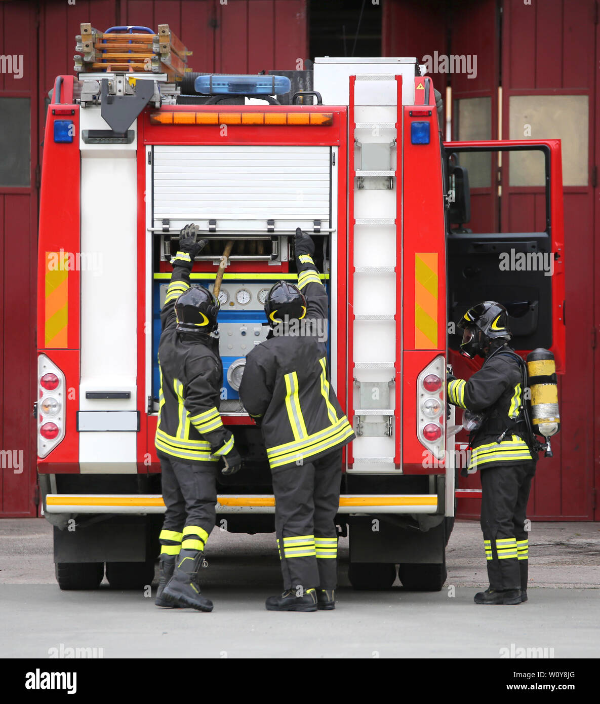 three firemen in action and the fire engine Stock Photo - Alamy