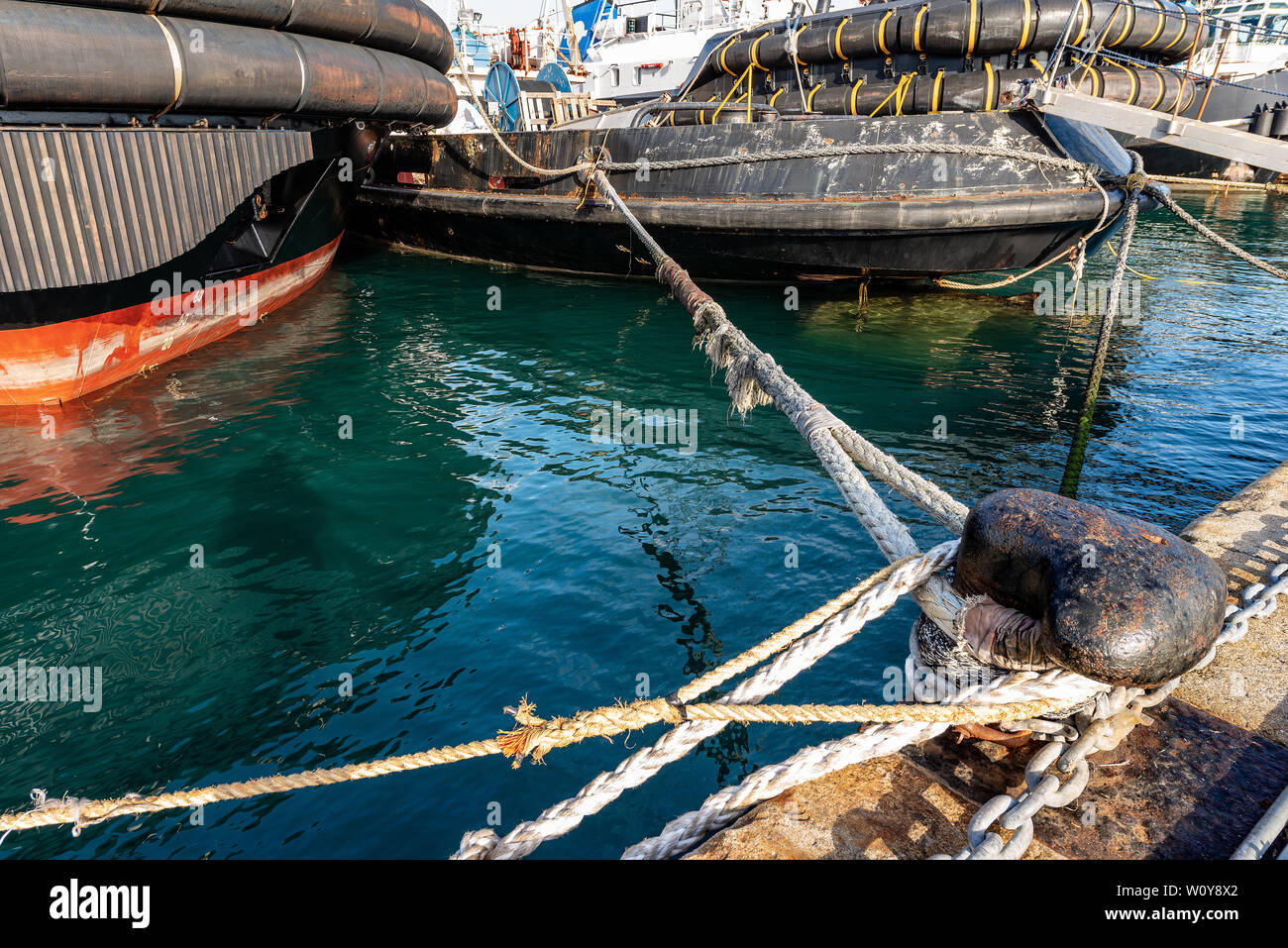 Ships moored in the port - Large black mooring bollard with ropes or ...