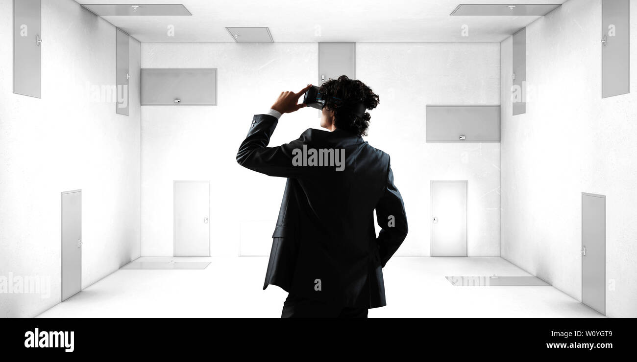 Back view of a young businessman in virtual reality headset in a room ...