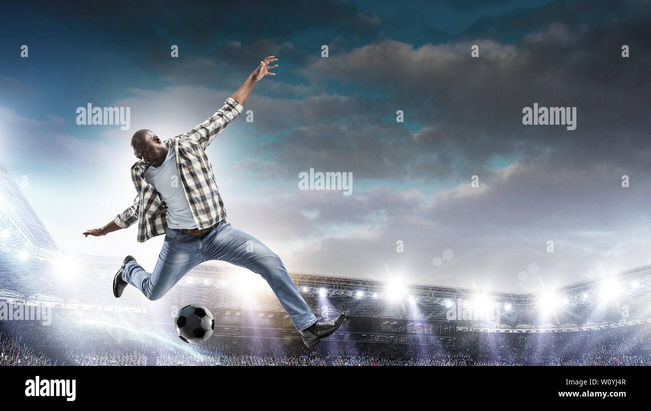 Black Man in casual clothes plays football alone on a full stadium ...