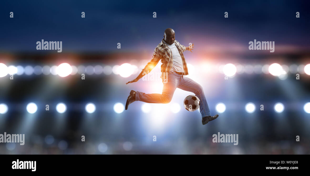 Black Man in casual clothes plays football alone on an full night ...