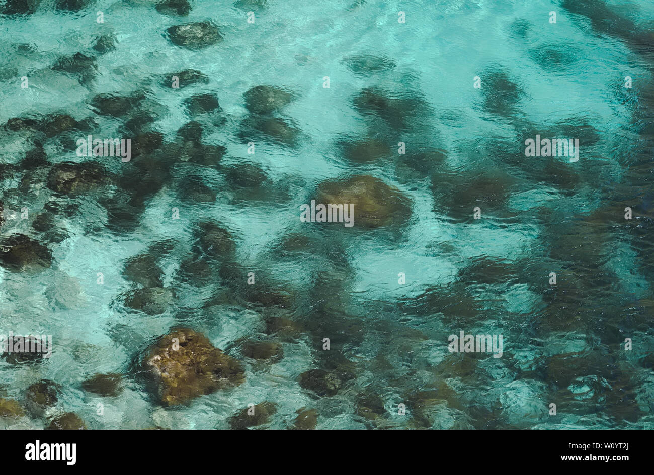 Close up of rocks on the sea floor looking through clear blue water ...