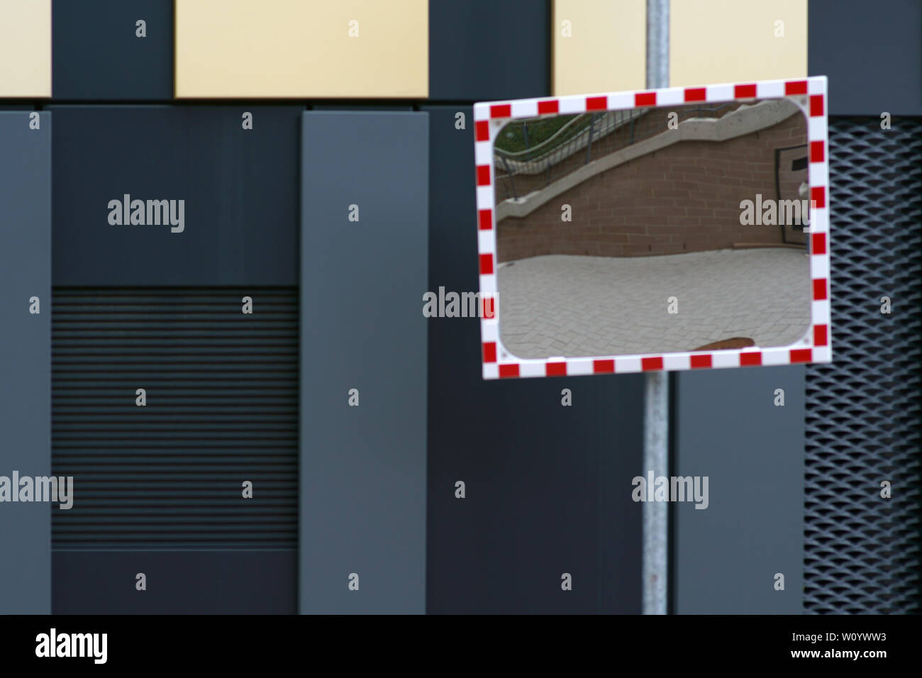 On the wall of a house with a modern facade, a traffic mirror hangs ...