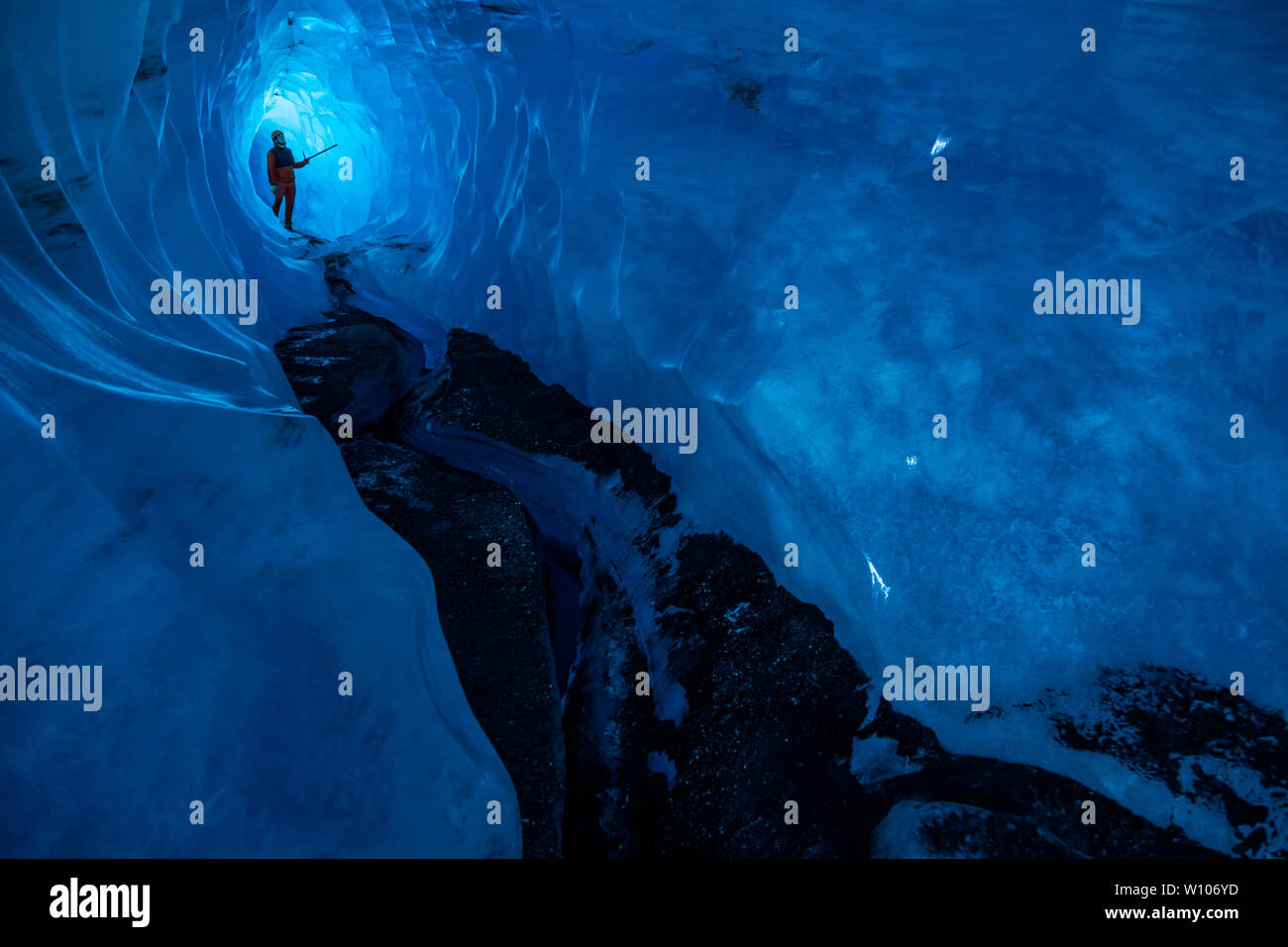 A deep, dark ice cave with a man standing in the back. He is ...