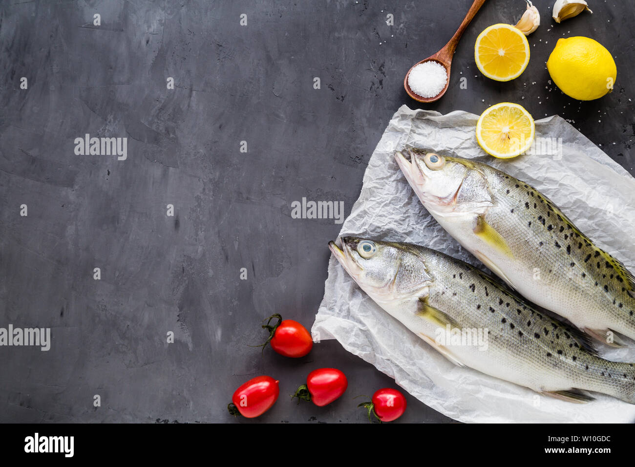 Fresh raw fish with spices, lemon, salt on dark stone background ...
