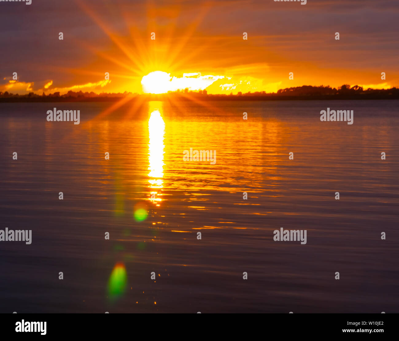 Dramatic sunrise through dark cloudy sky over bay with lens flare Stock ...